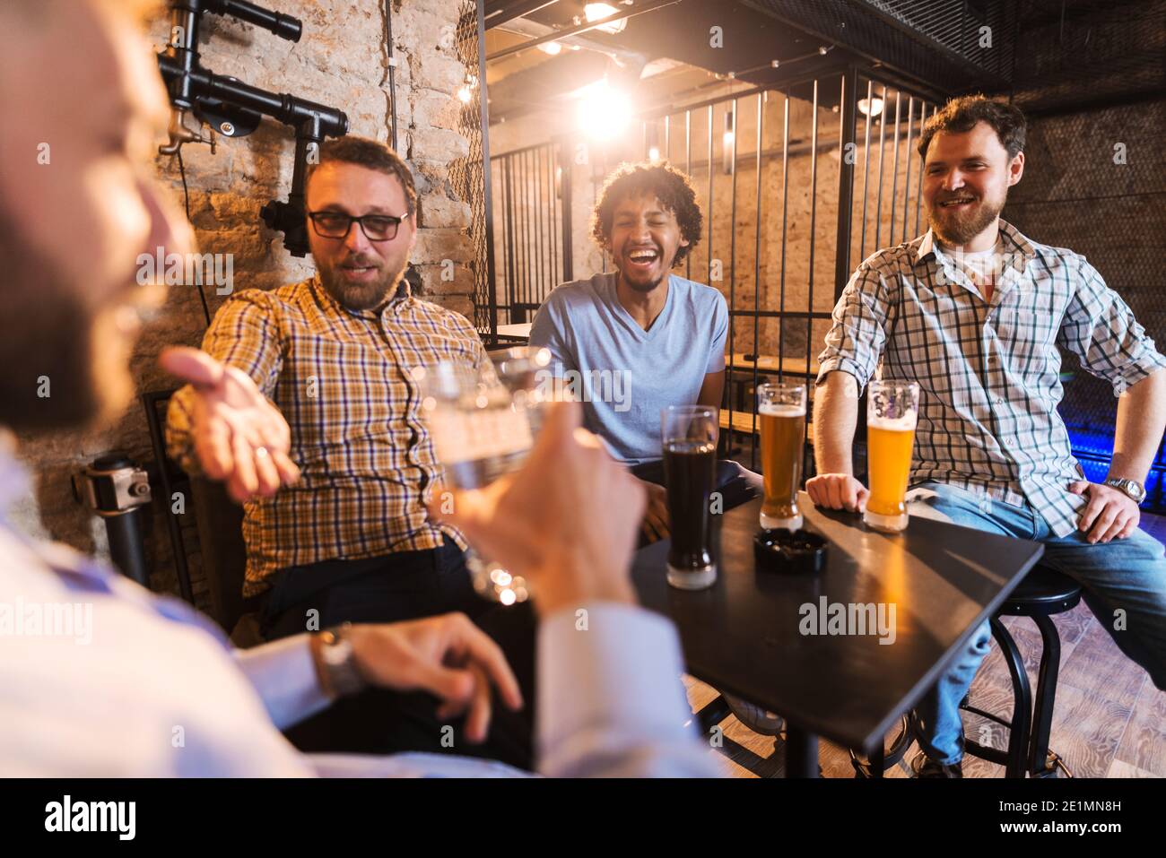 Group of friends talking and drinking beer while sitting in pub ...