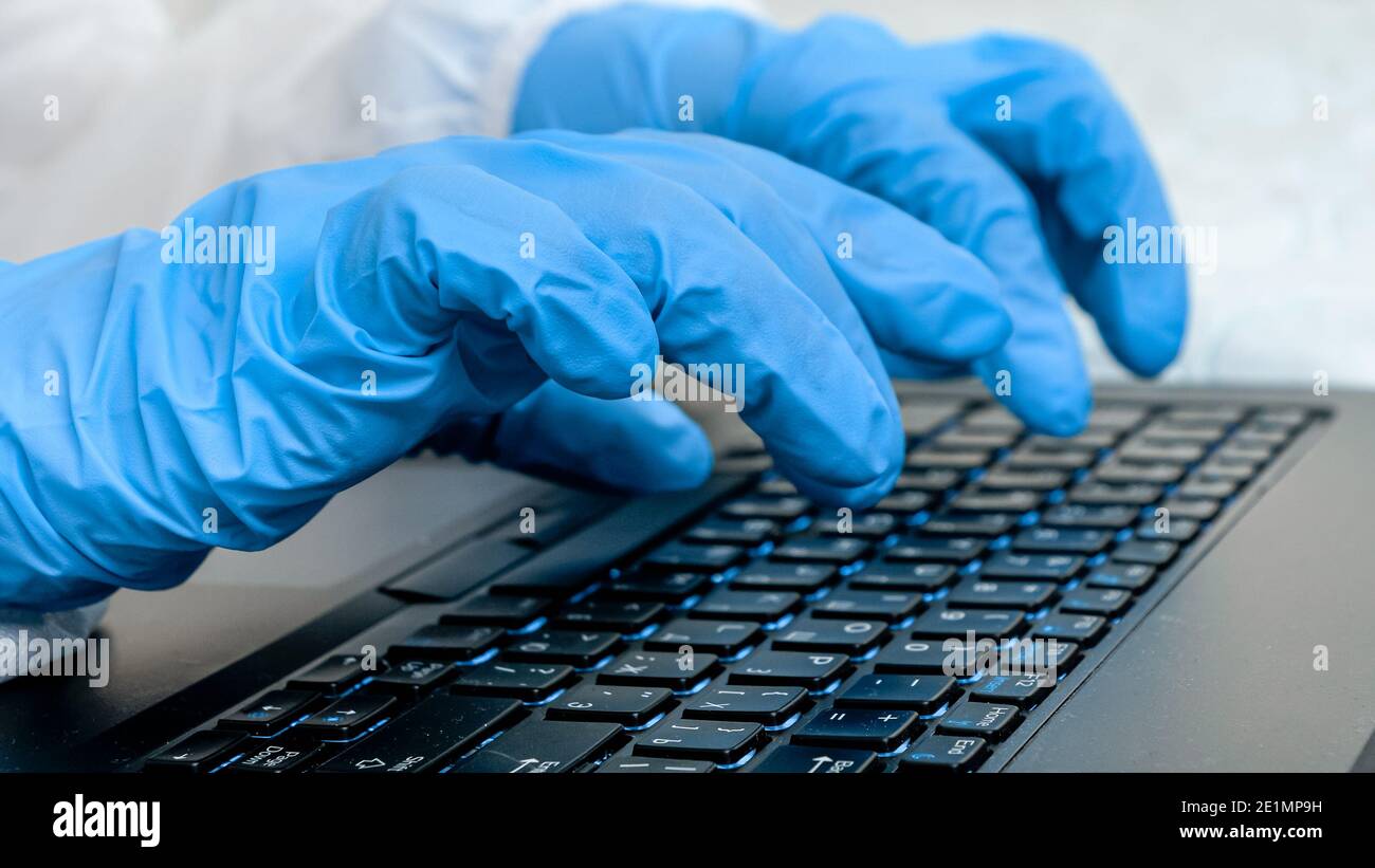 Closeup of doctor in protective rubber gloves working on laptop. Typing ...