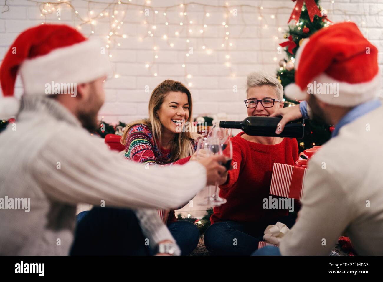 Two young couples celebrating christmas together. Sitting on a floor ...