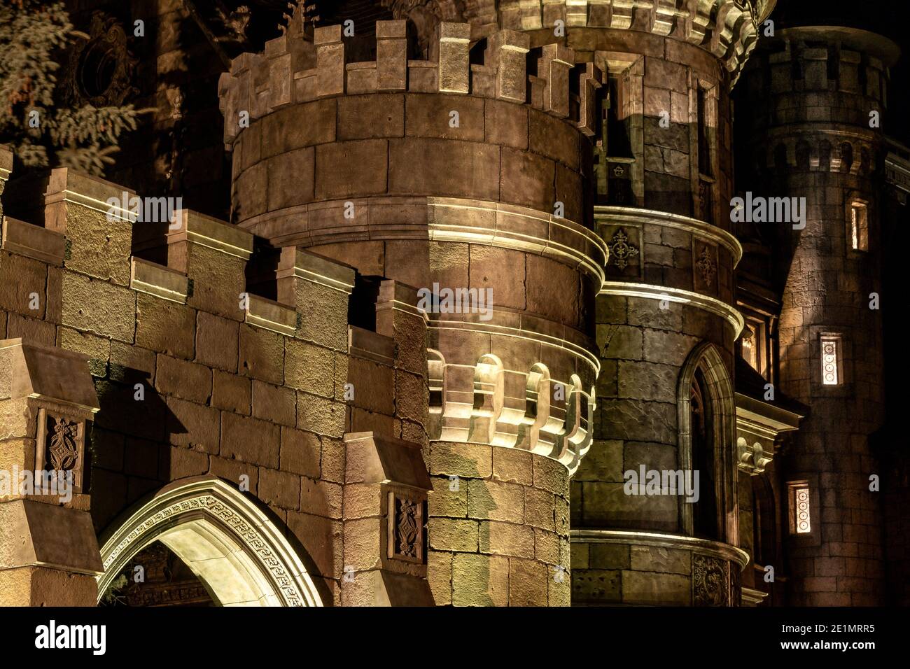 Round watchtowers at the gates of the stone castle wall at night lights ...
