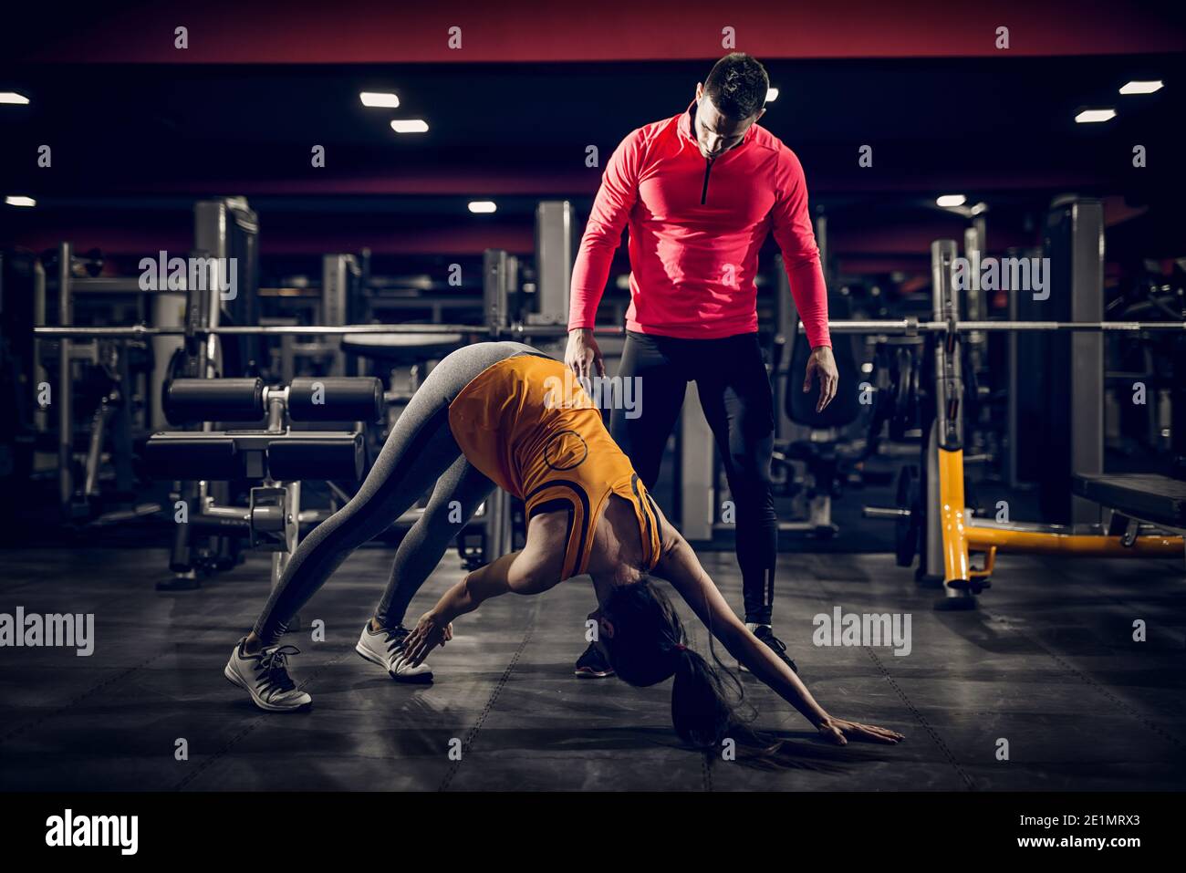 Young motivated female working out in a gym with help of a personal ...