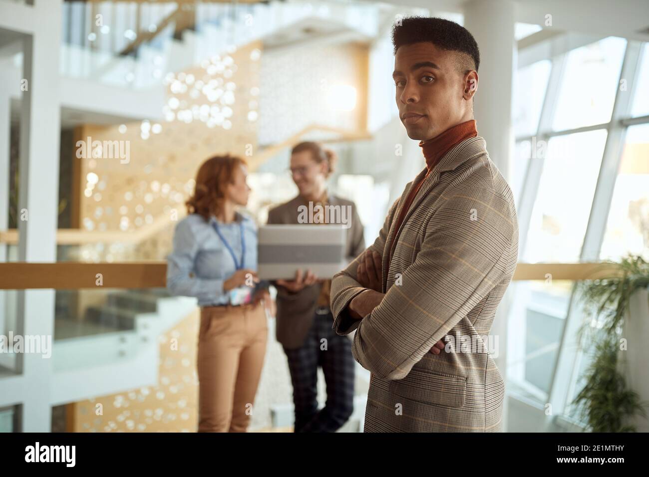 A young male employee standing at company's hallway and posing for a ...