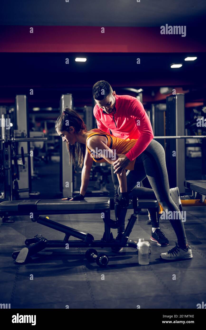 Motivated young sporty female trying to lift weight with a assistance ...