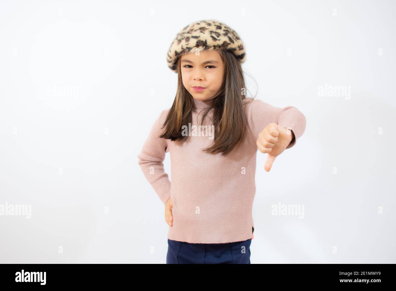 Little girl with pink sweater doing bad signal over white background ...
