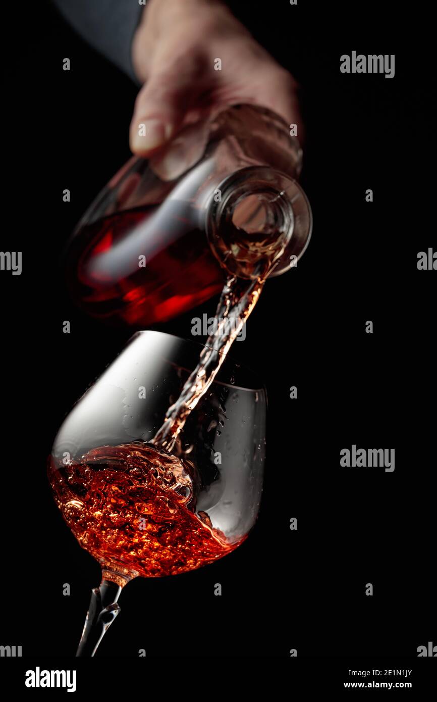Pouring brandy in a glass goblet. Black background with copy space ...