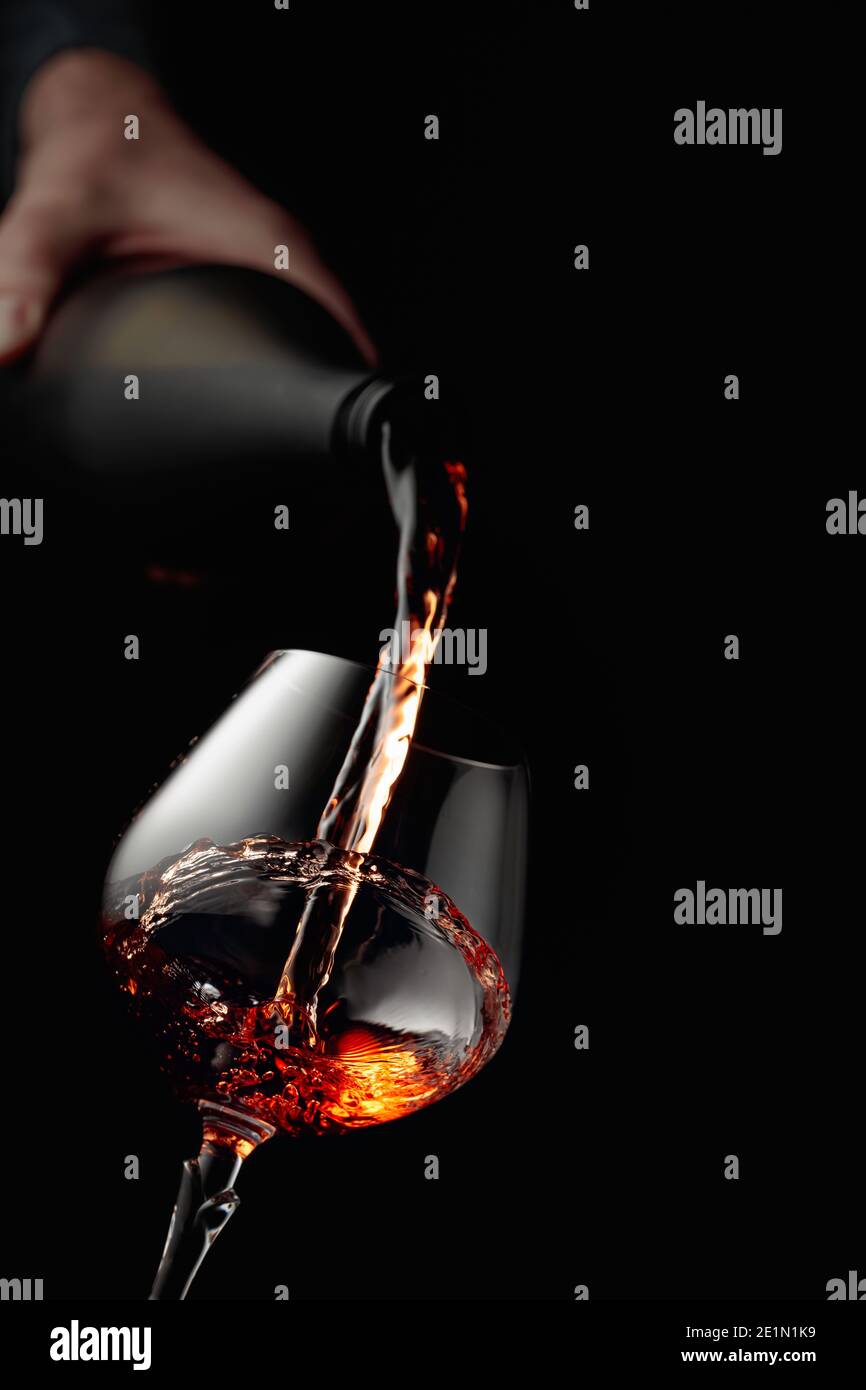 Pouring brandy in a glass goblet. Black background with copy space ...