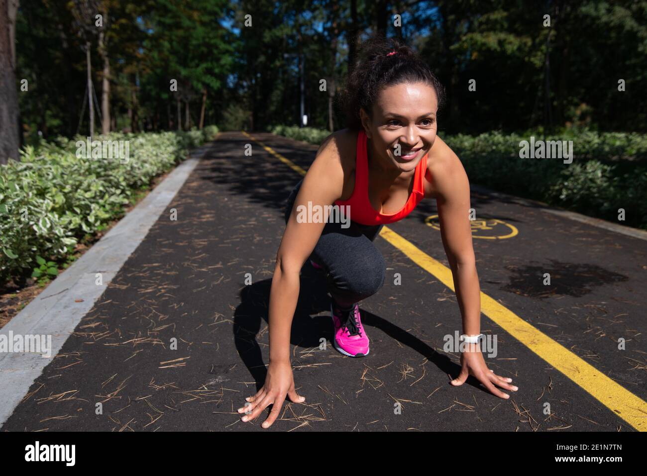Attractive smiling runner woman on the start position on a running way ...