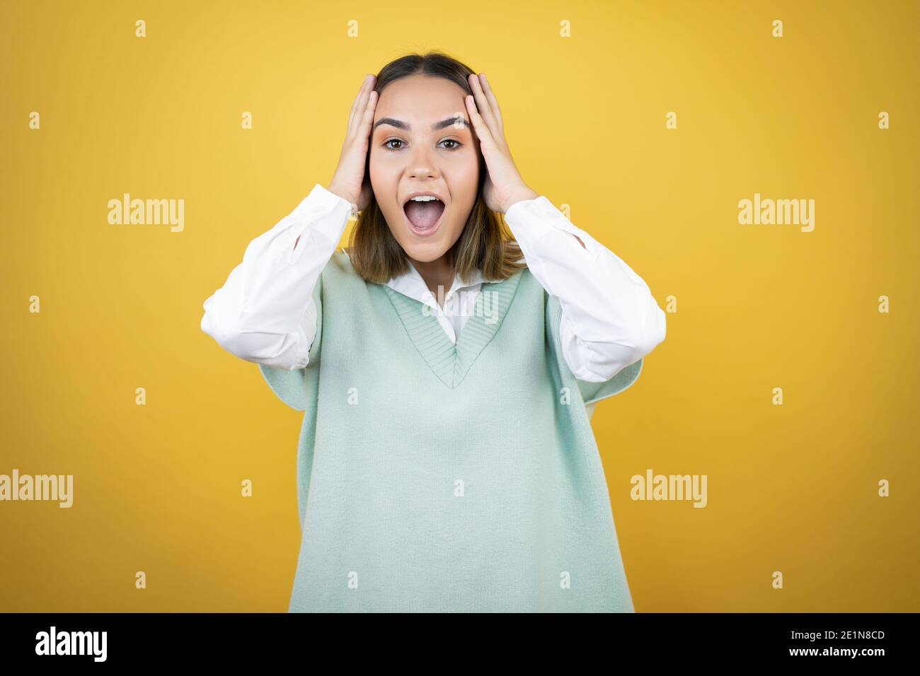 Pretty young woman standing over yellow background crazy and scared ...