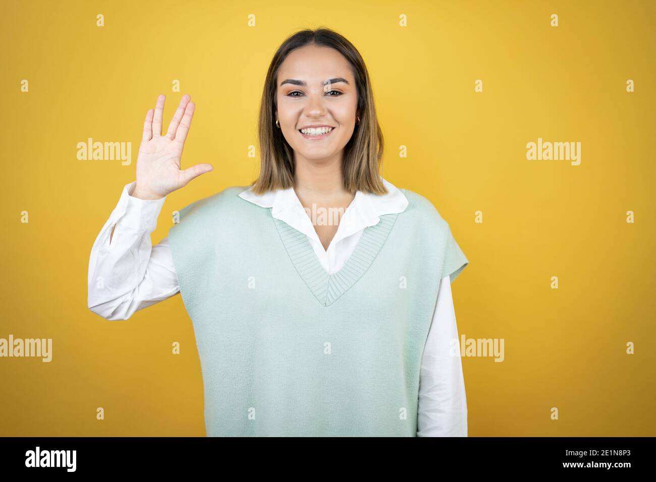 Pretty young woman standing over yellow background doing star trek ...