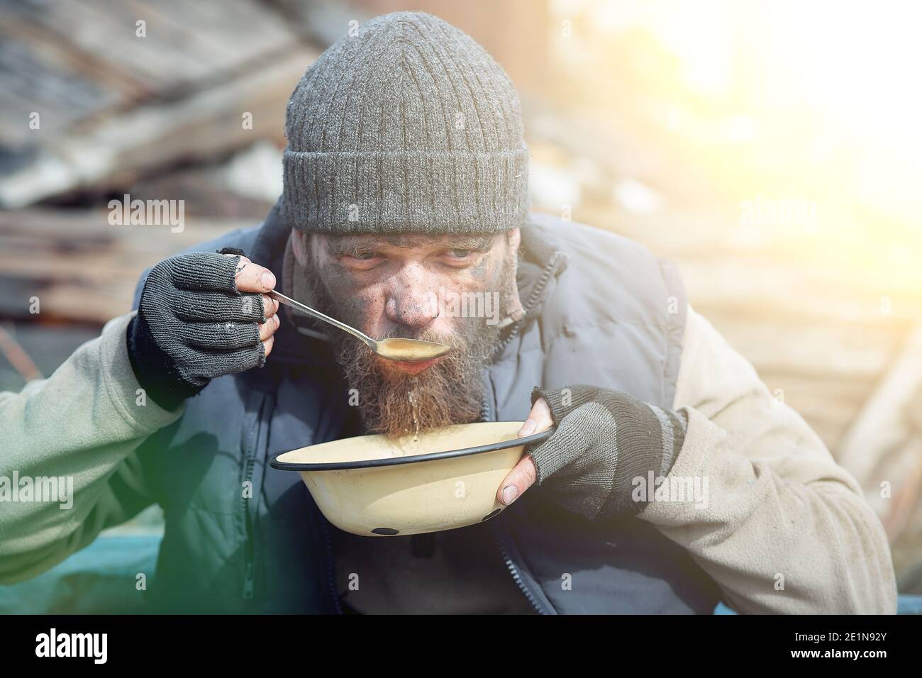 a homeless man eats soup from a plate near the ruins, helping poor and ...
