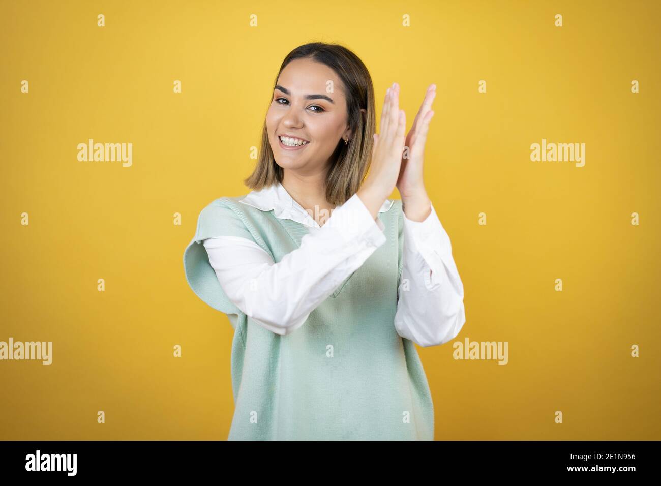 Pretty young woman standing over yellow background clapping and ...