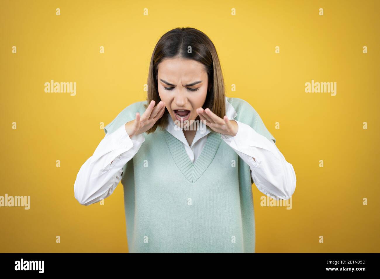 Pretty young woman standing over yellow background shouting and ...