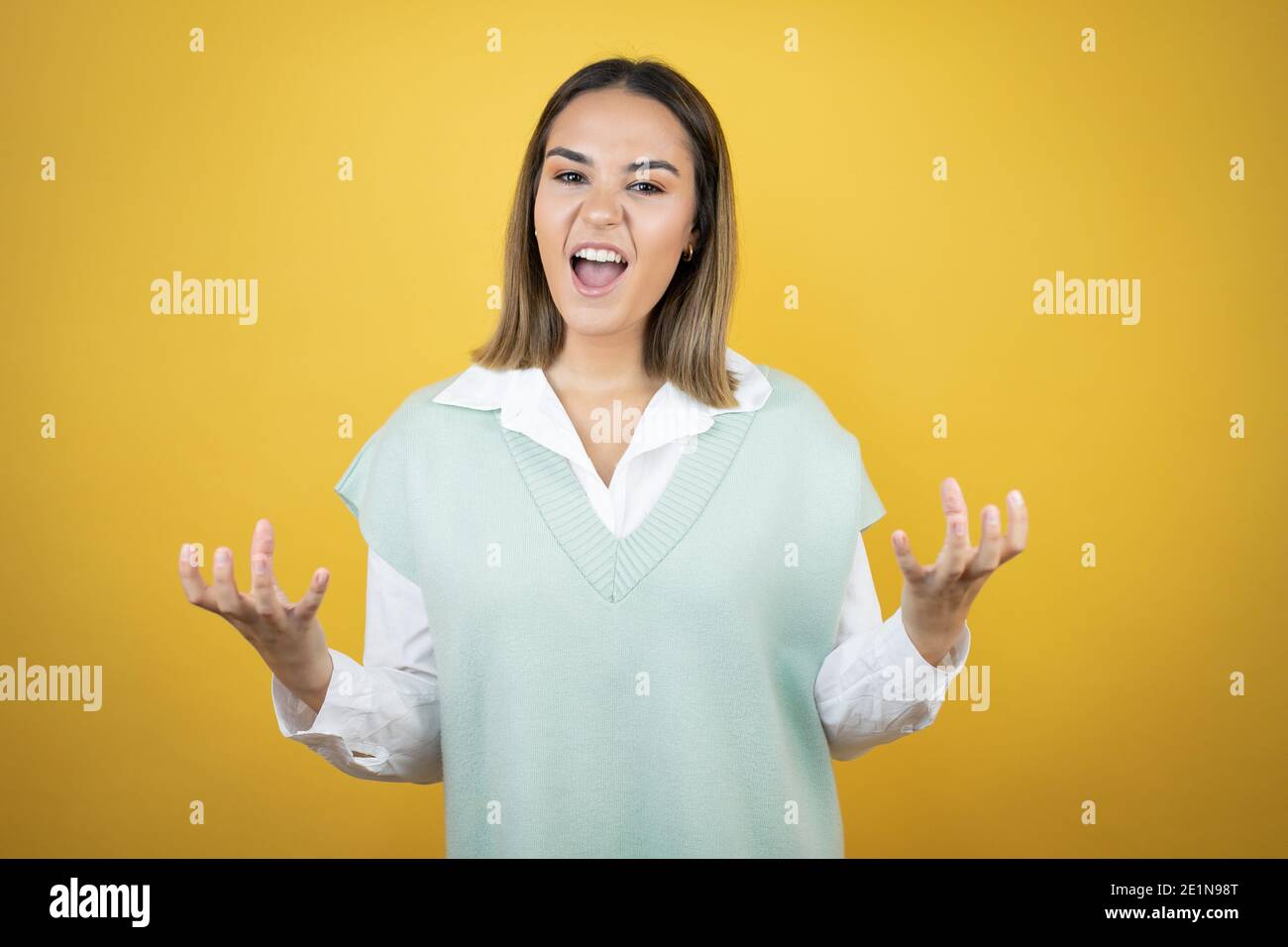 Pretty young woman standing over yellow background crazy and mad ...