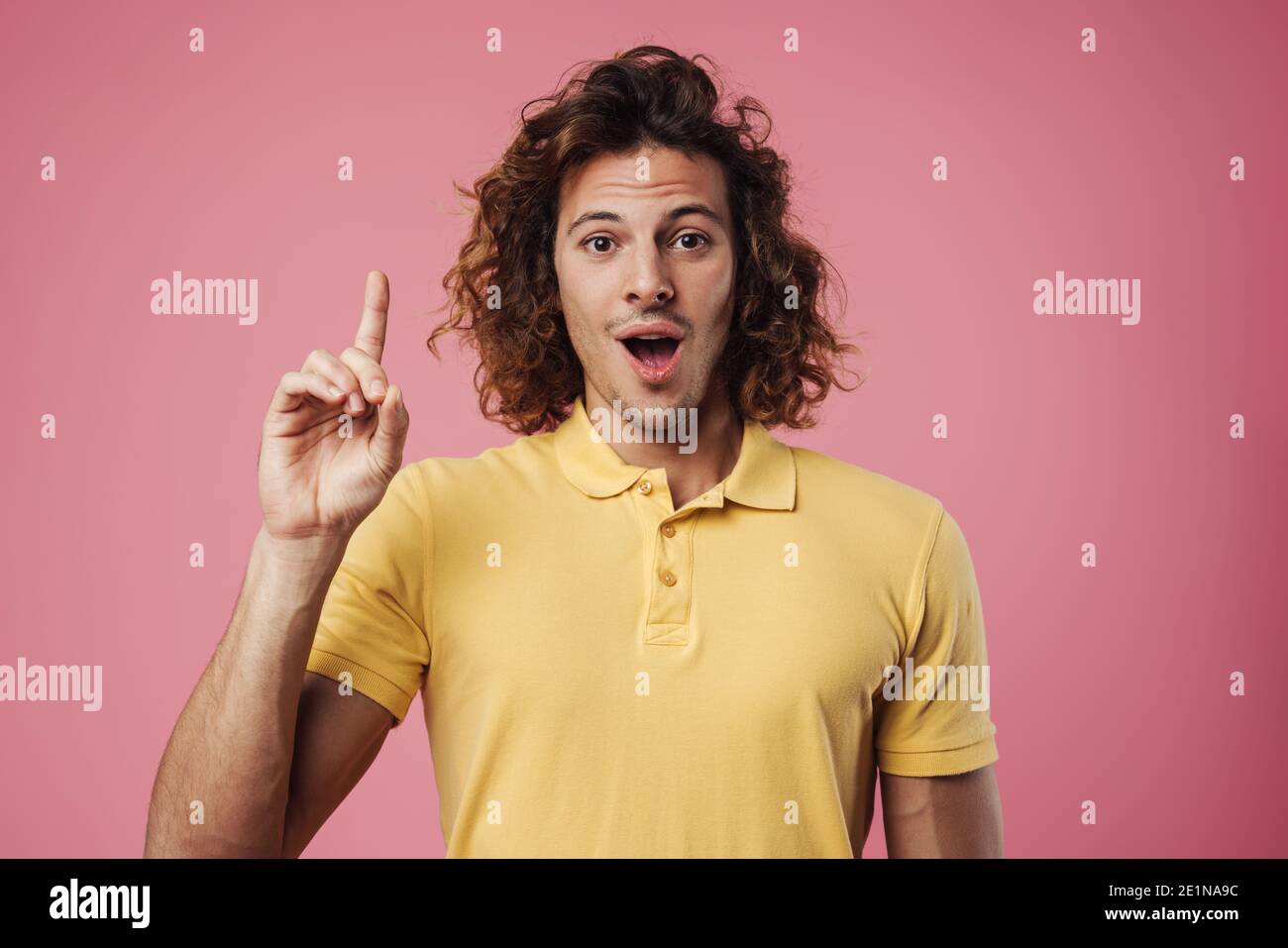 Shocked handsome unshaven guy pointing finger upward isolated over pink ...