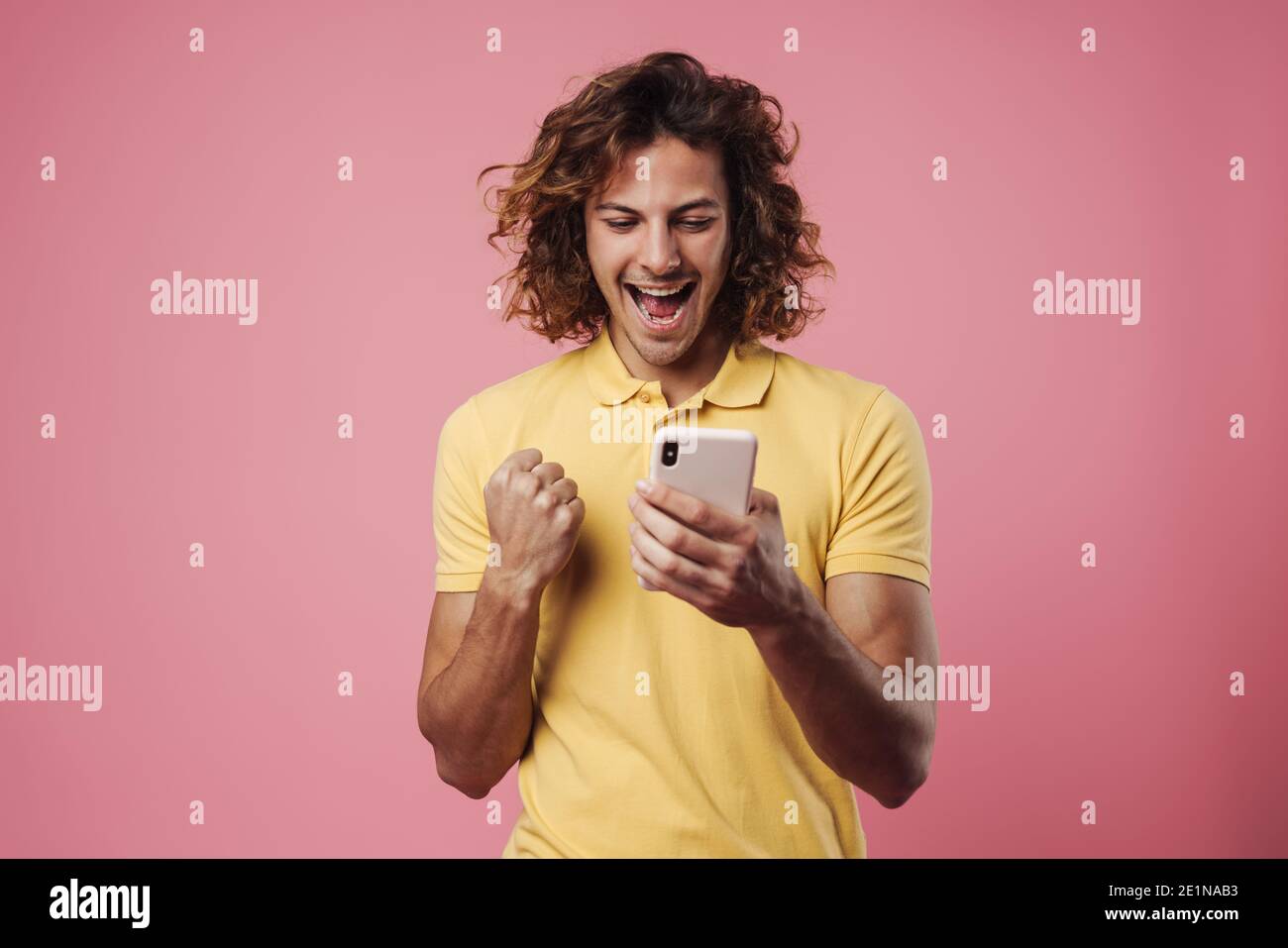 Portrait of an excited young man using mobile phone isolated over pink ...