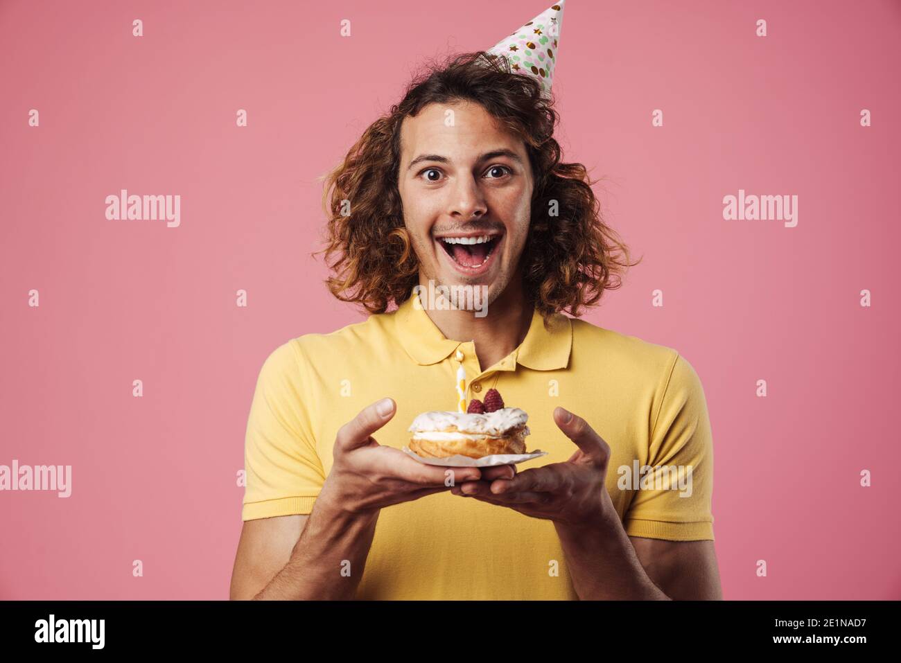 Excited handsome guy in party cone posing with birthday cake isolated ...