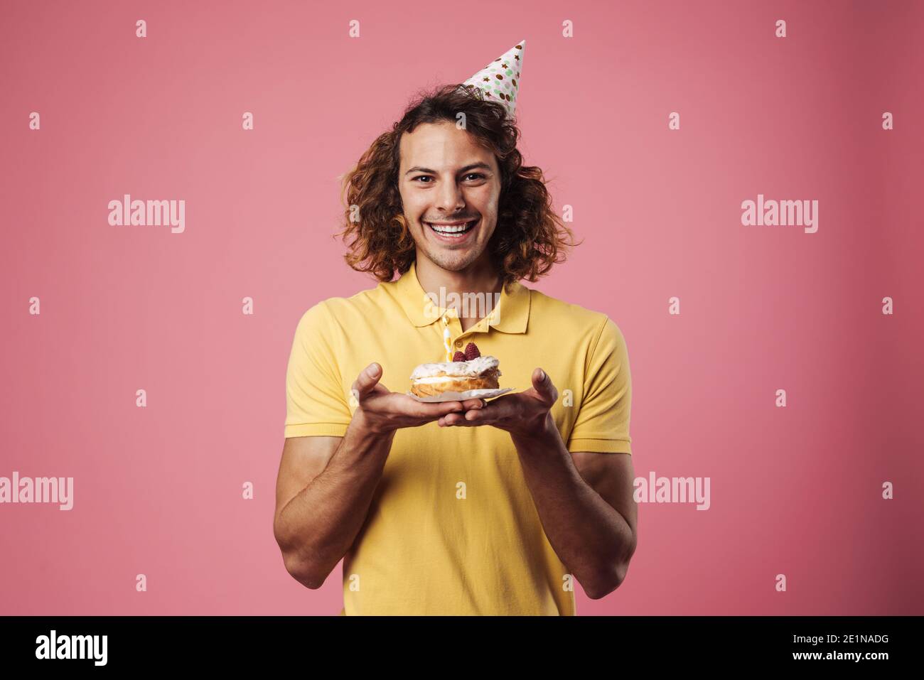 Cheerful handsome guy in party cone posing with birthday cake isolated ...