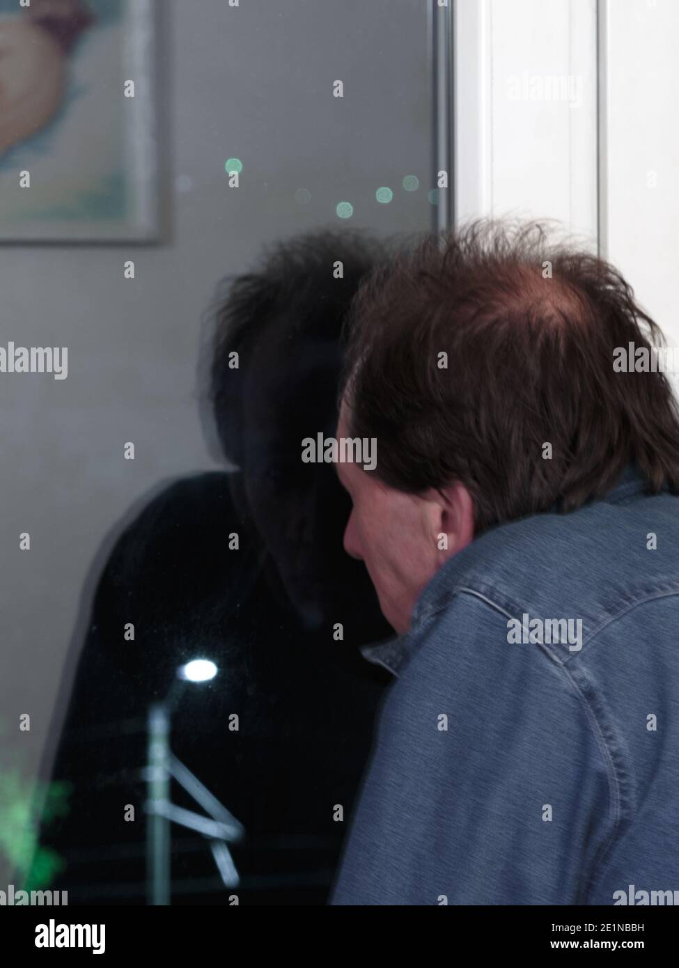 A lonely man looks through the window at night. Its shadow is reflected ...