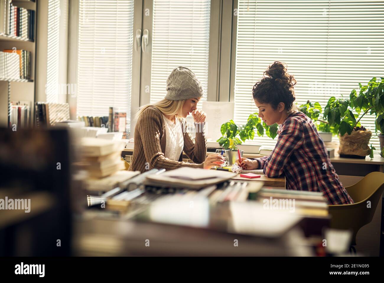 Two young focused student girls sitting in a library and studying ...