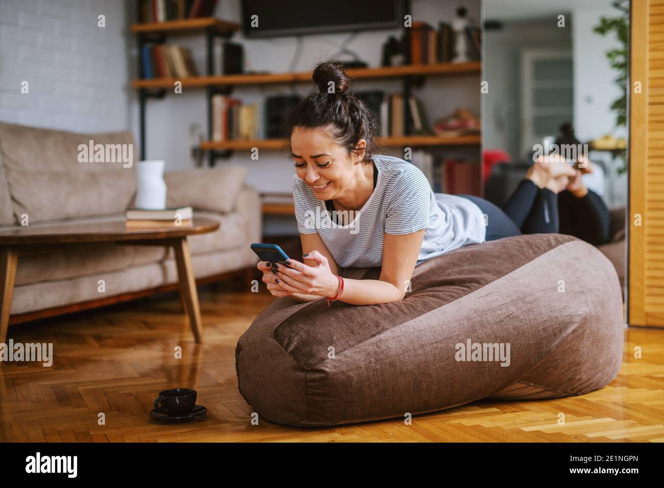 Woman lying on lazy bag and using smart phone for texting. Living room ...