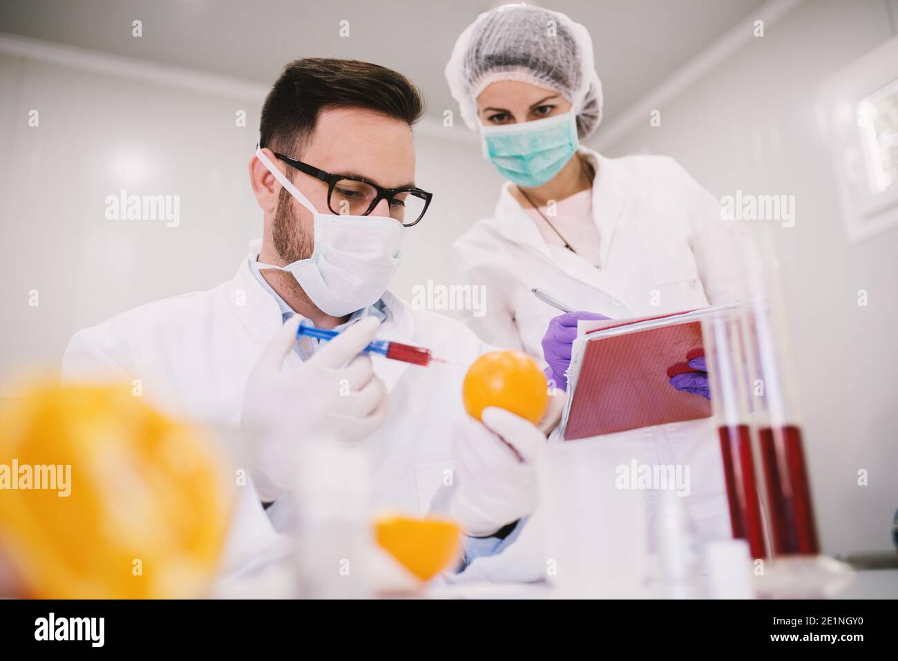 Employees in a lab taking a sample from orange with syringe Stock Photo ...