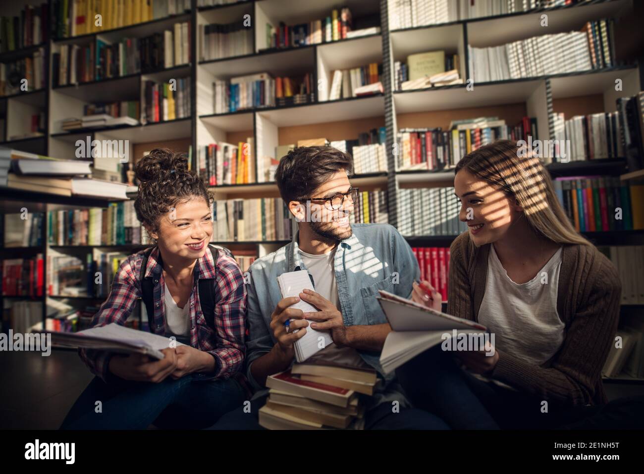 Three cheerful hard working students sitting on a library floor and ...