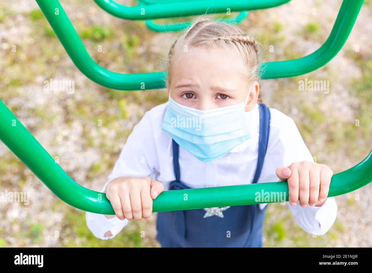 Girl in a protective mask on her face at the playground looks into the ...