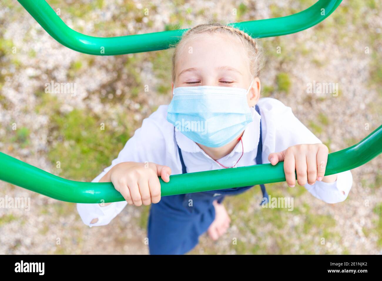 Caucasian girl in a protective face mask on the playground with closed ...