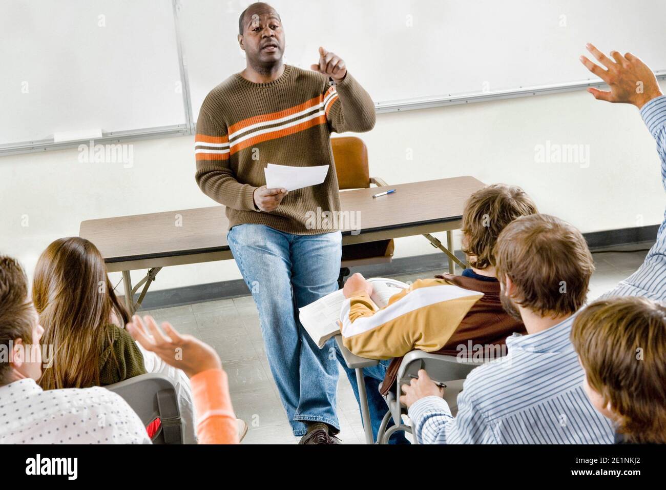 Professor pointing at college student with hands raised in classroom ...