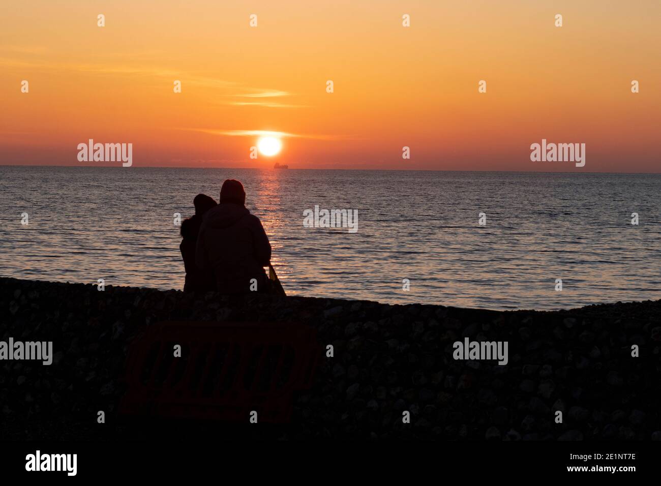 Couple watching the sun setting over the sea at Brighton, East Sussex ...