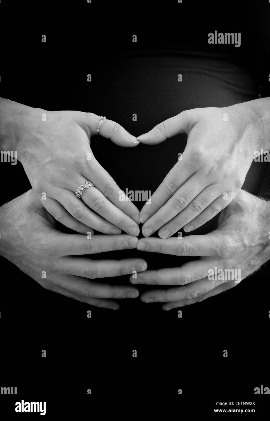 Pregnant women with partner forming hand shaped heart on the bump Stock ...