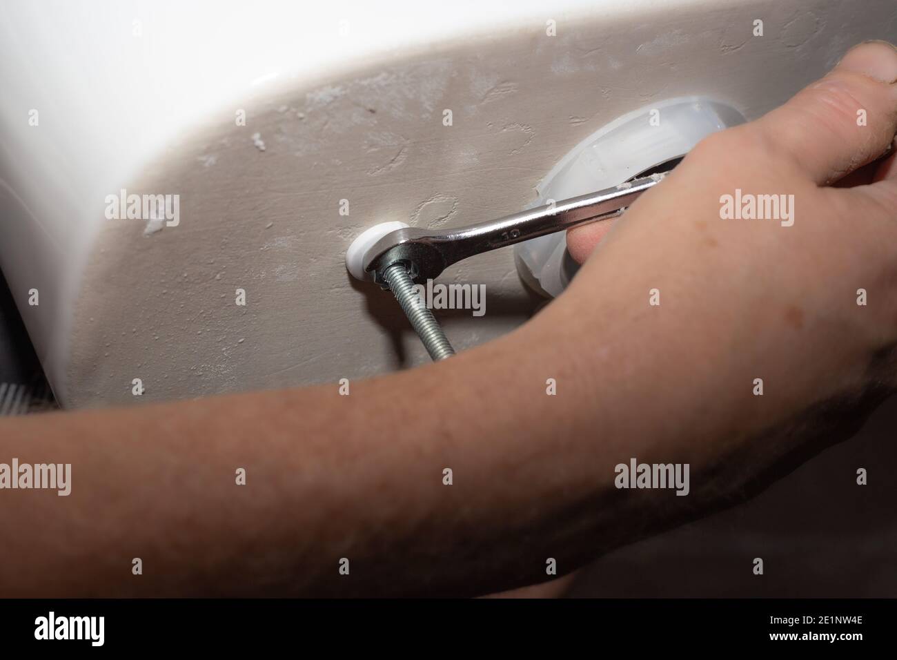 Assembly and installation of the toilet. A man with a wrench tightens ...