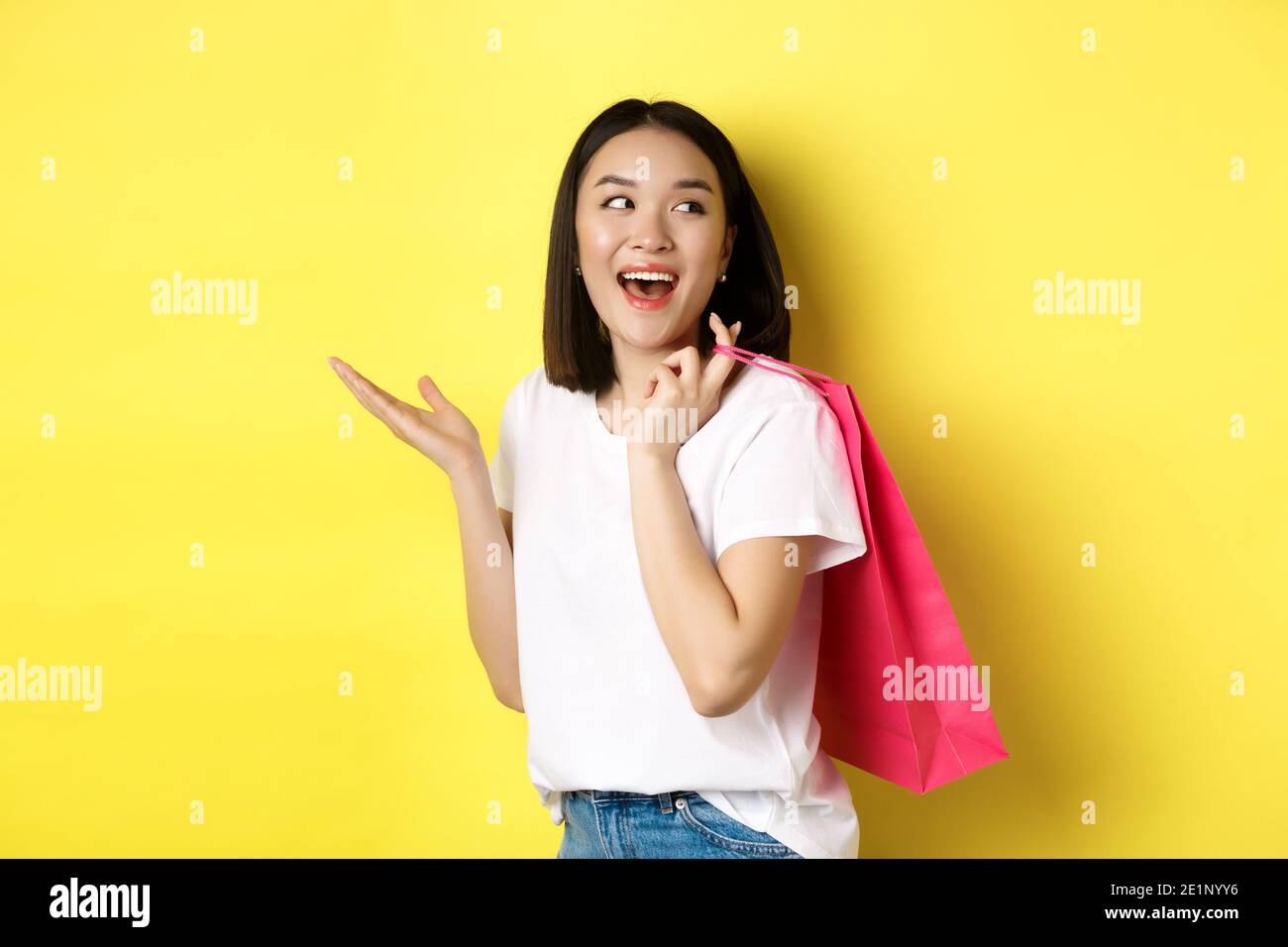 Cheerful asian female shopper looking amused, holding shopping bag and ...