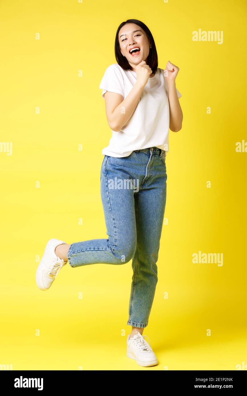 Full size shot of happy asian woman dancing and jumping from happiness ...