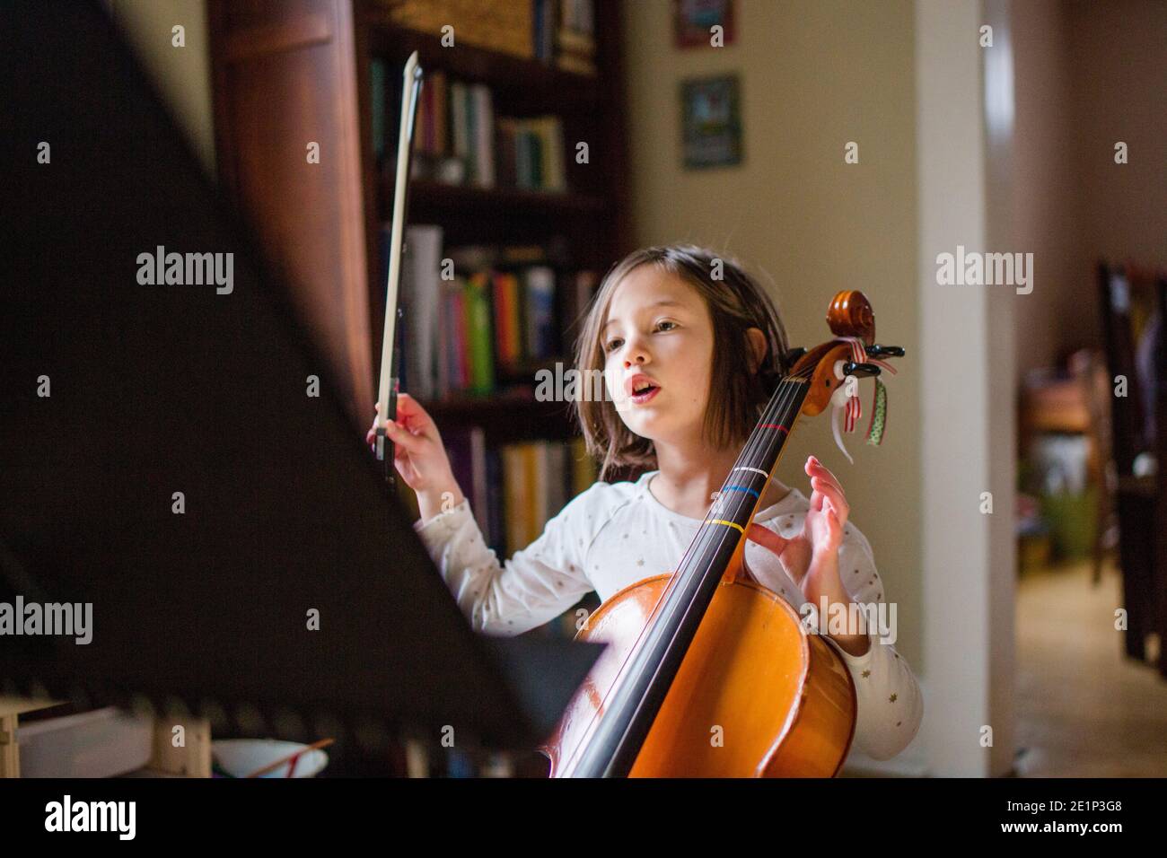 a little girl holding cello lifts her bow up in preparation to play ...