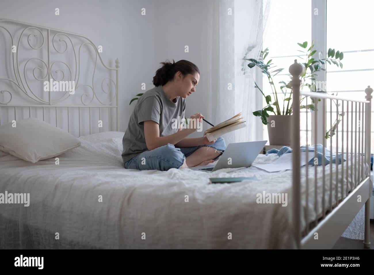 Female student reading notes on bed preparing for session during online ...
