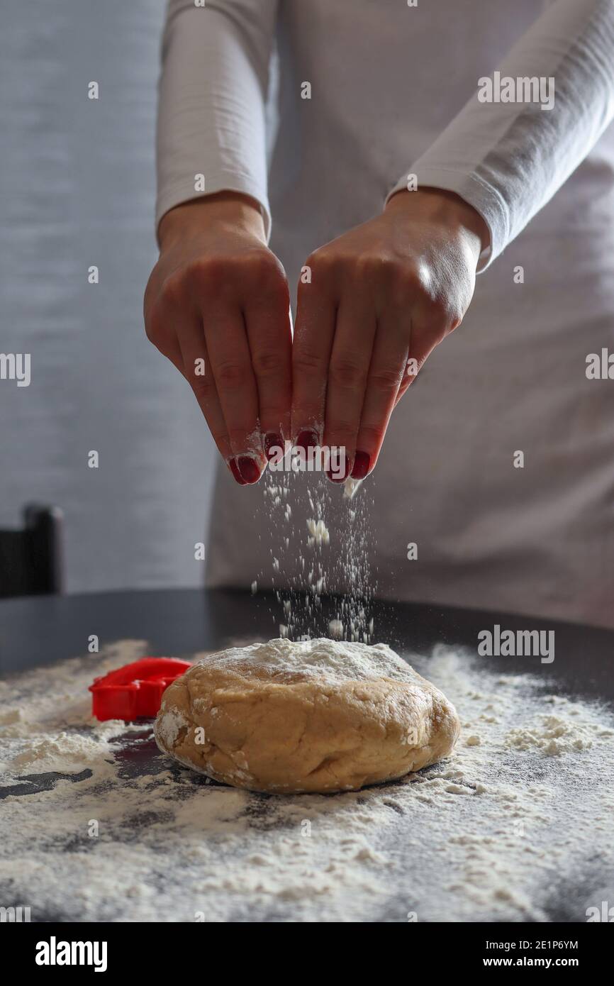 Female hands sprinkle flour on cookie dough for cookies on the table ...