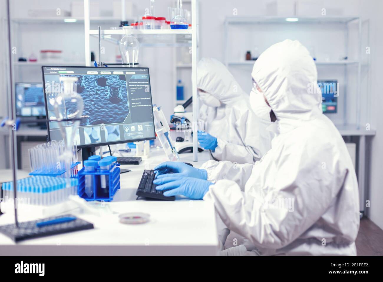 Lab engineer typing on pc conducting experiment in laboratory dressed ...