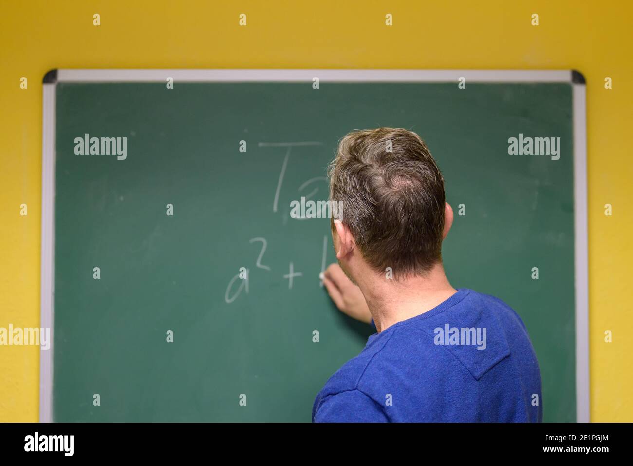Mathematics teacher standing with his back to the camera writing a ...