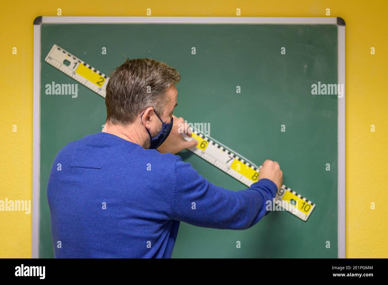 Back view of a teacher using a ruler to draw a straight diagonal line ...