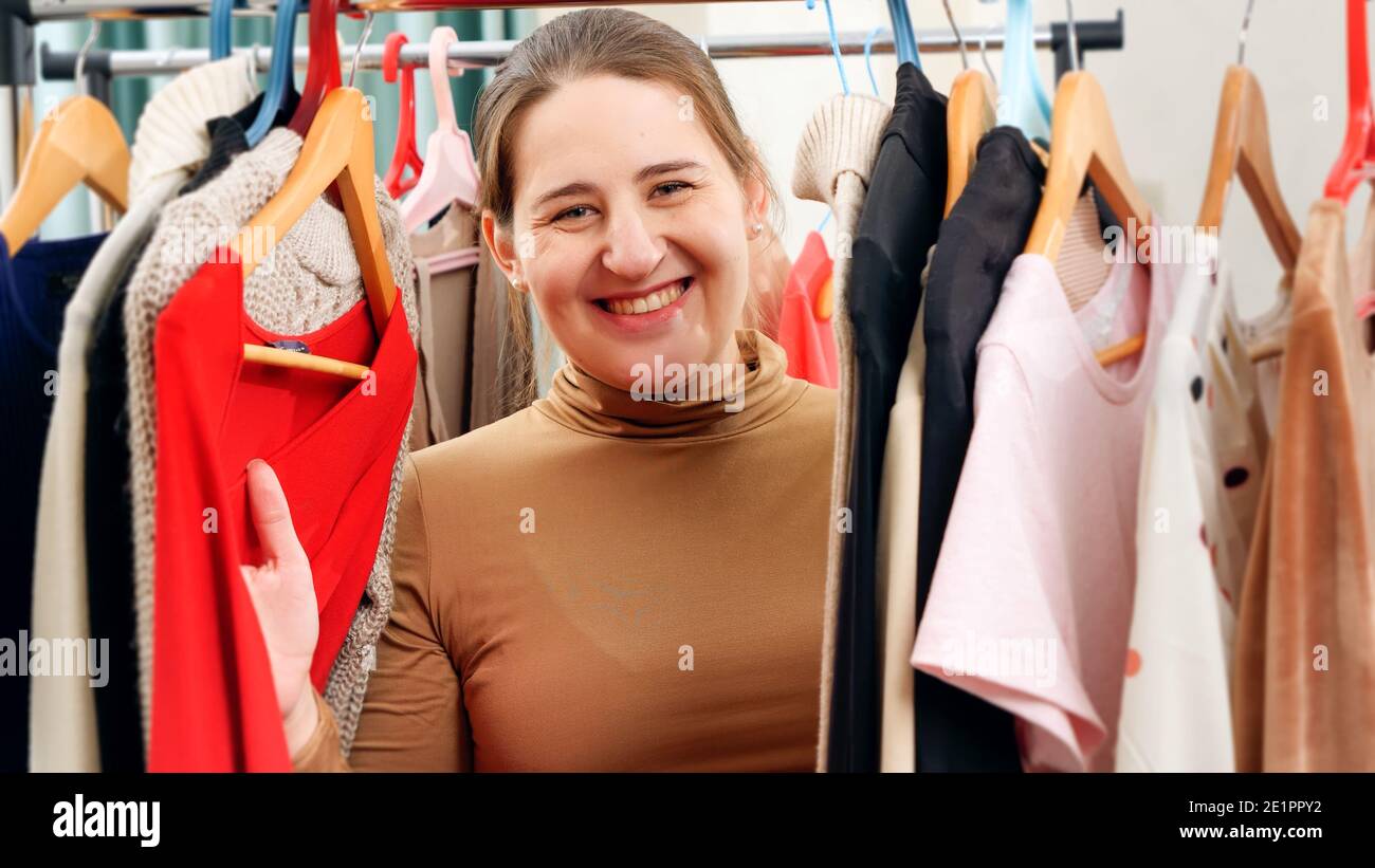 Beautiful smiling woman behind long rack of clothes on hangers choosing ...