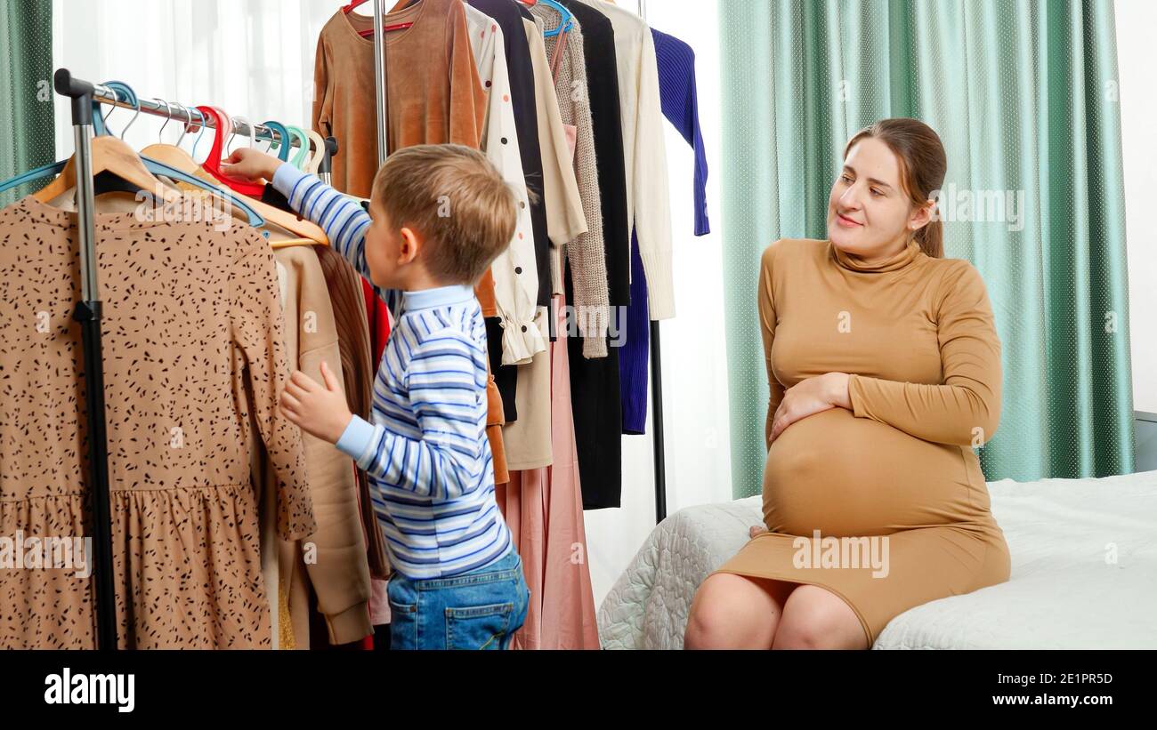 Happy smiling boy taking clothes from clothes rack ad giving it his ...