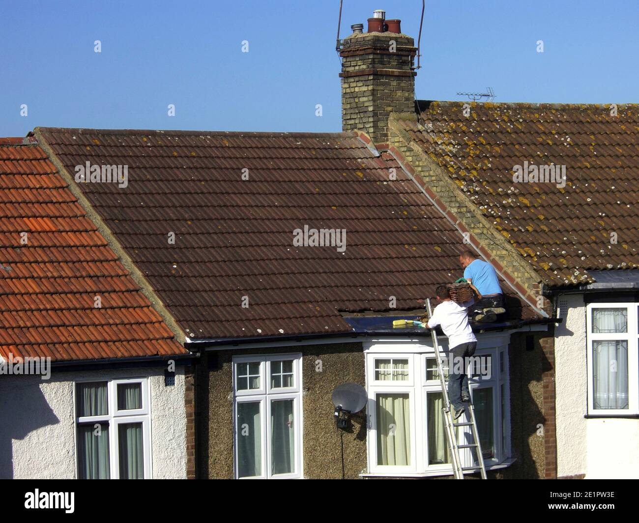 building work, roofers carrying roofing tiles on ladder to repair roof ...