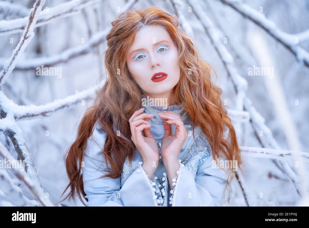 Young redhead woman, a princess, walks in a winter forest in a blue ...