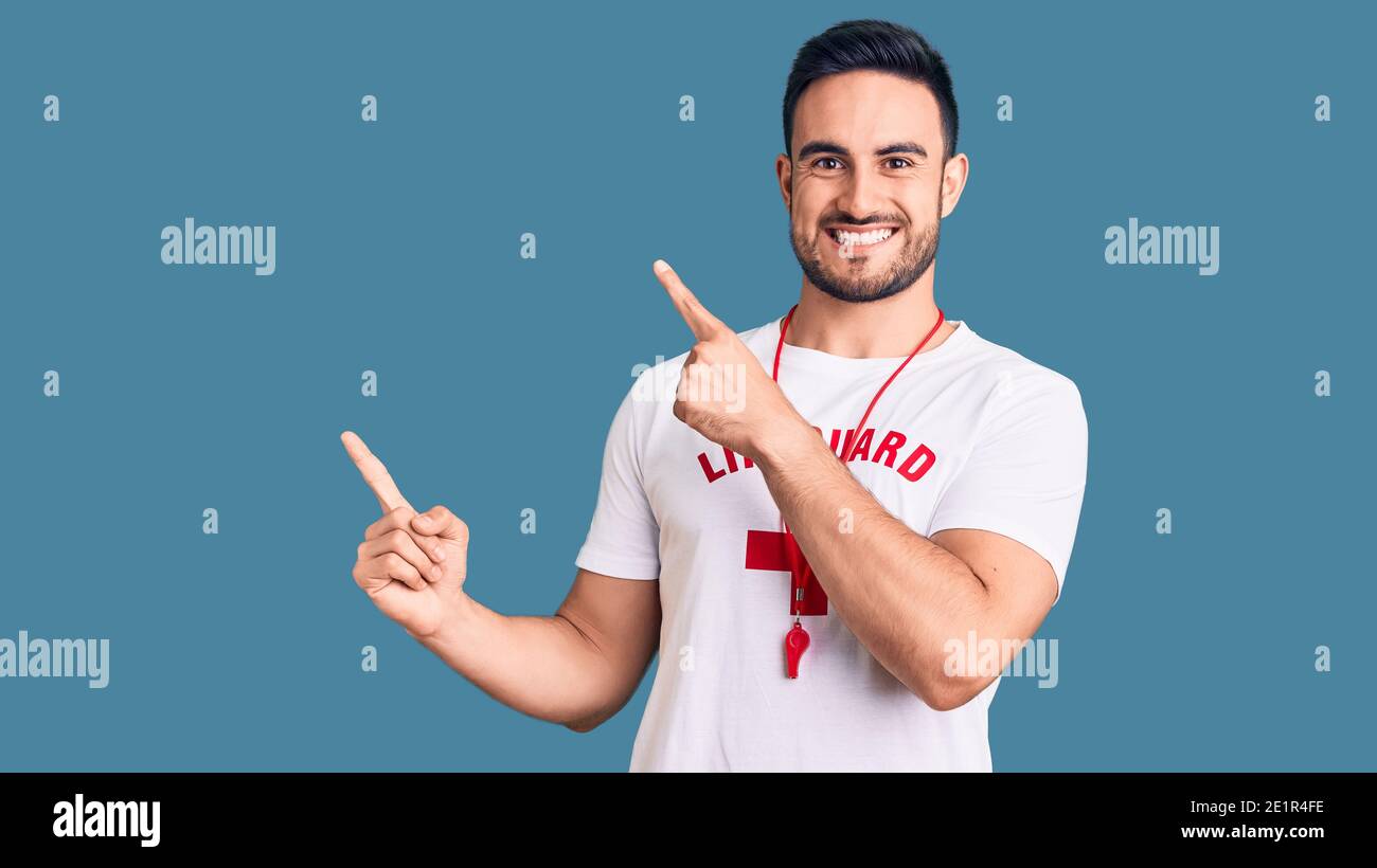 Young handsome man wearing lifeguard uniform smiling and looking at the ...