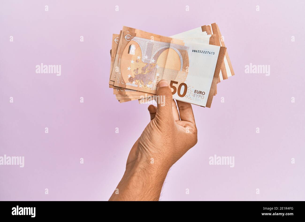 Hispanic hand holding 50 euro banknotes over isolated pink background ...