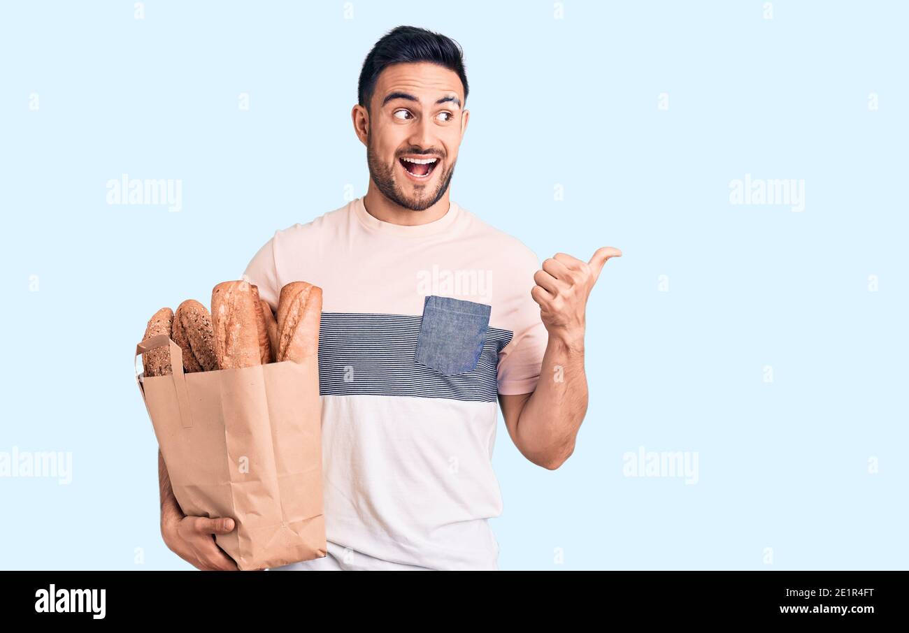 Young handsome man holding bread bag pointing thumb up to the side ...