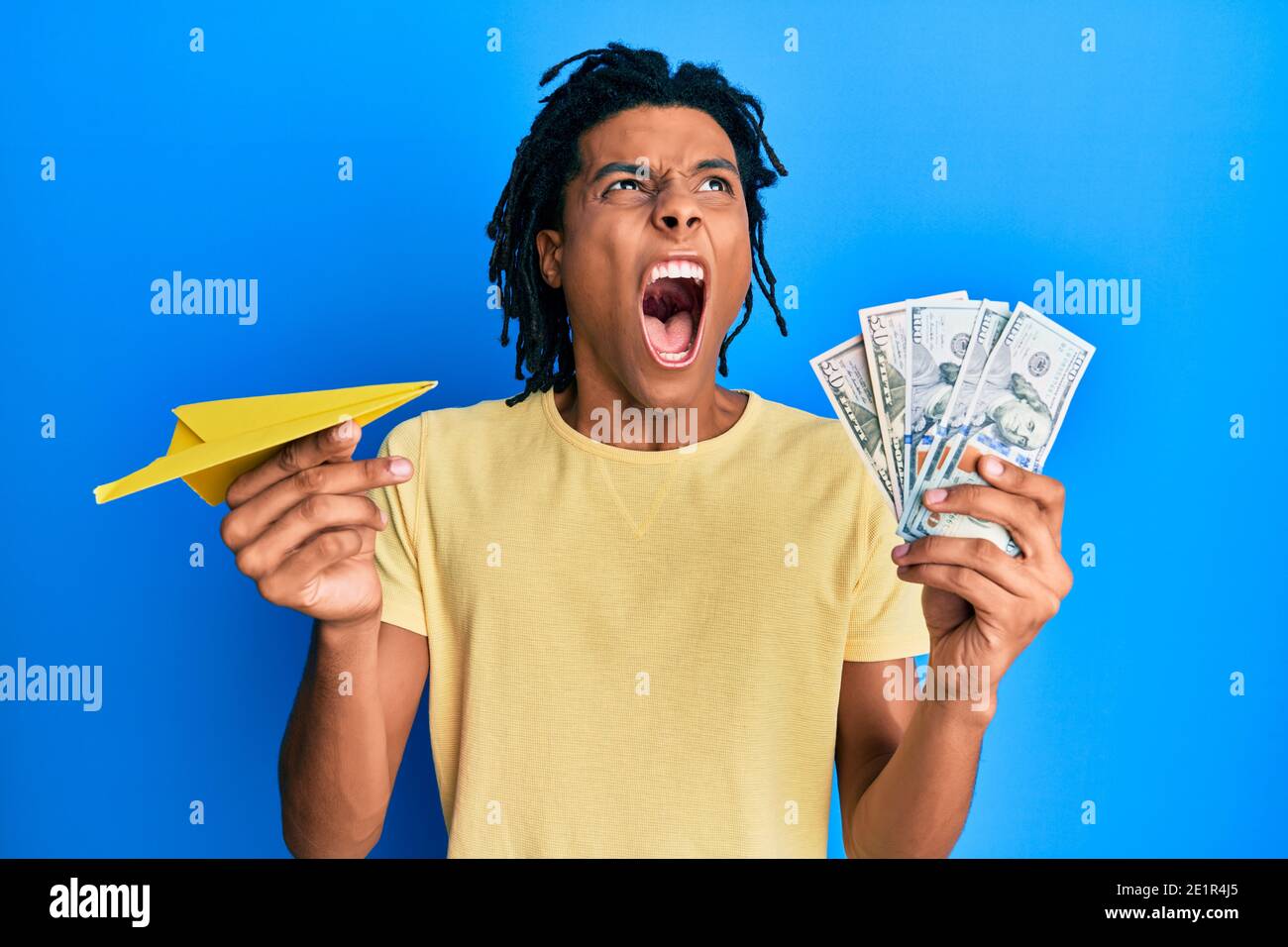 Young african american man holding paper plane and dollars angry and ...