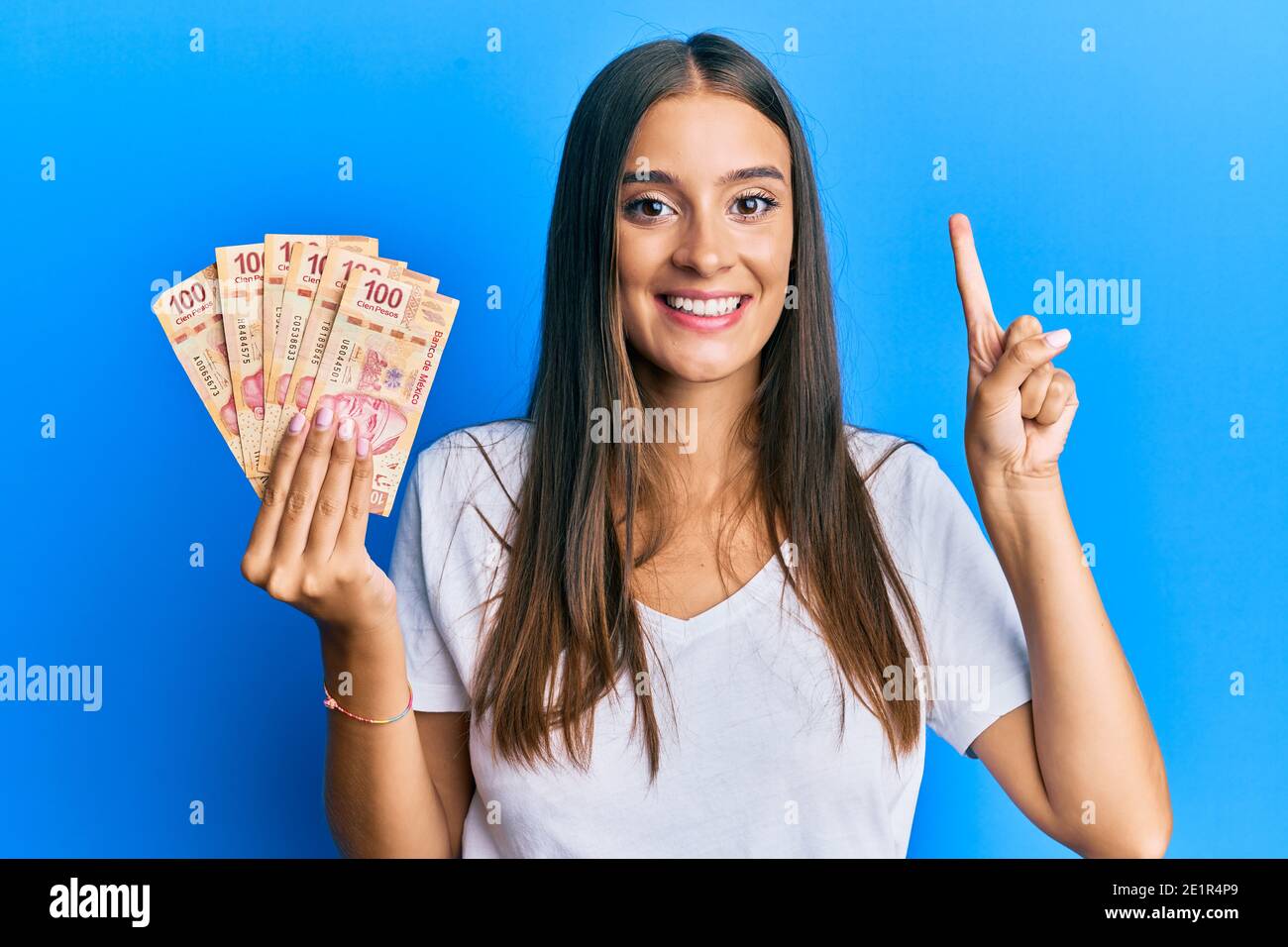 Young hispanic woman holding mexican pesos smiling with an idea or ...