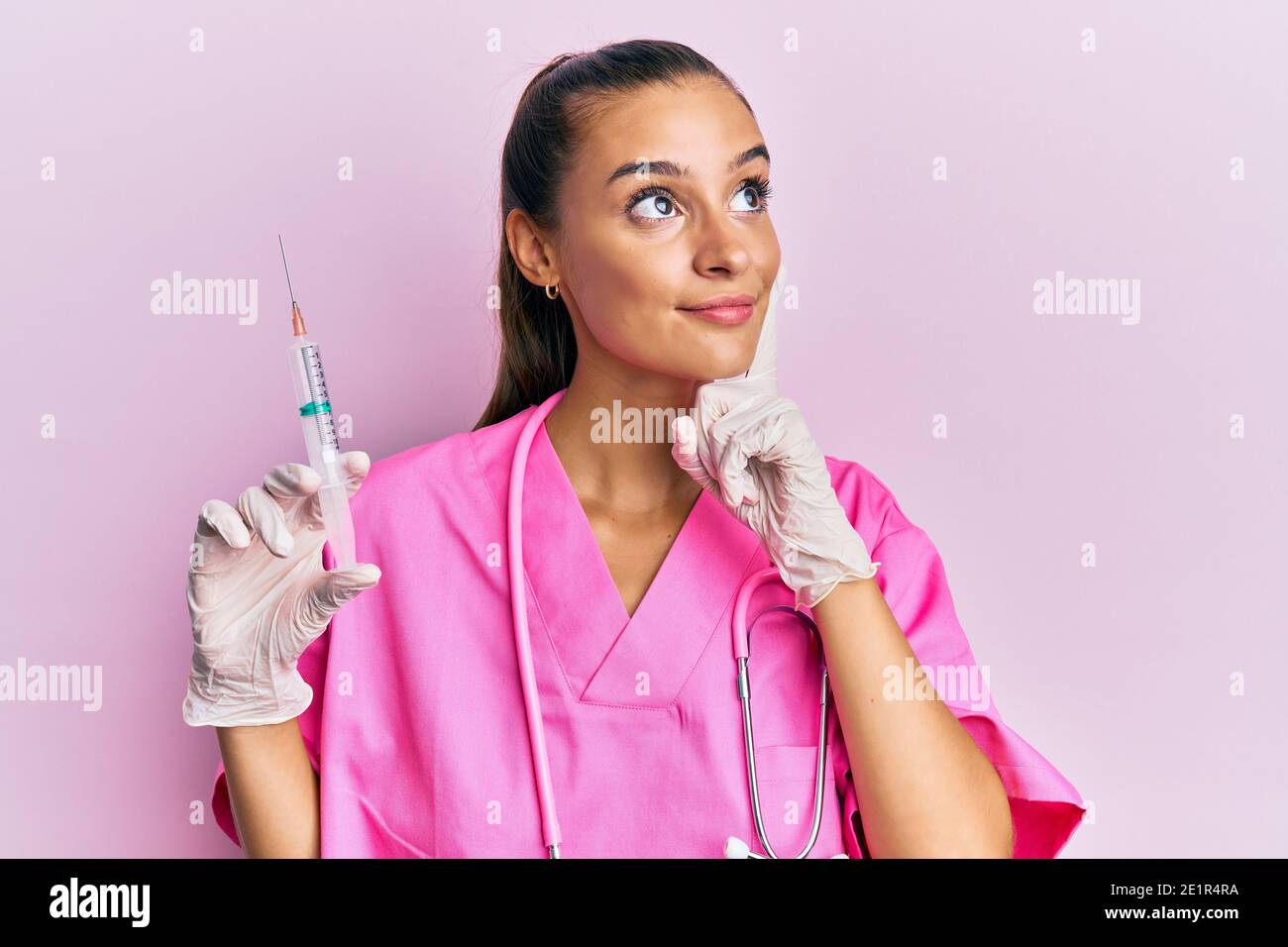 Young hispanic woman wearing doctor stethoscope holding syringe serious ...